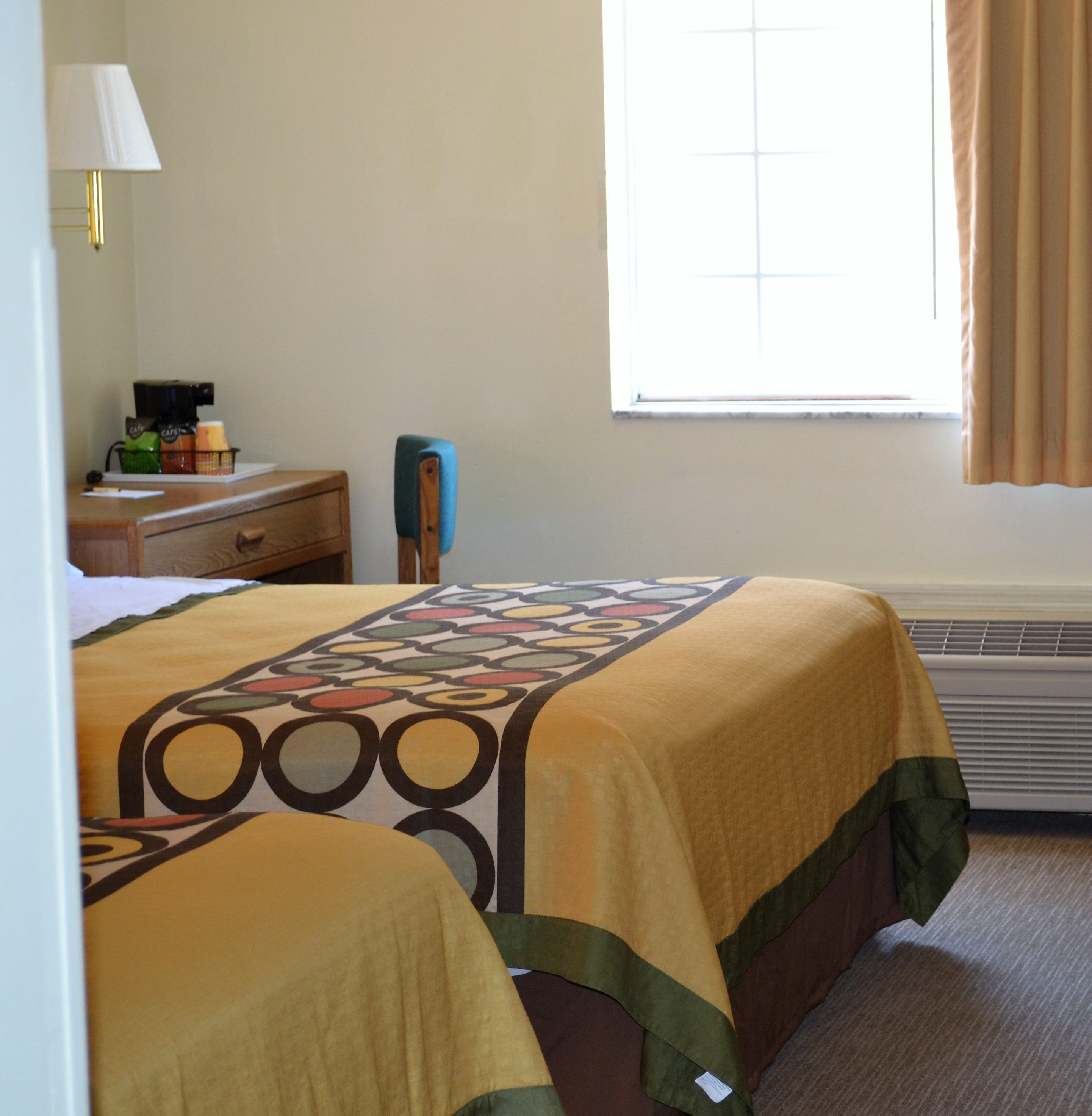 Quarto de hotel com cama, mesa de cabeceira, luminária, janela com cortinas e aquecedor.