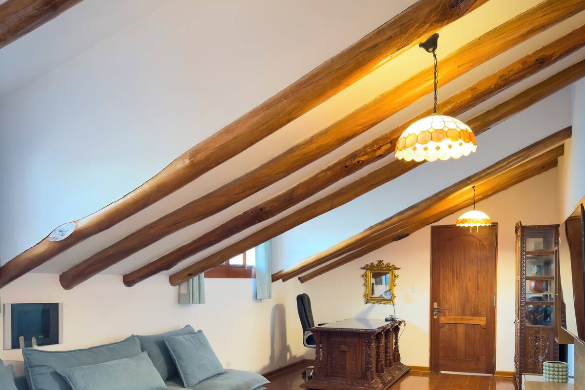 Um amplo loft com vigas de madeira aparentes, um sofá cinzento, uma mesa de centro de madeira e um armário de madeira com espelho.
