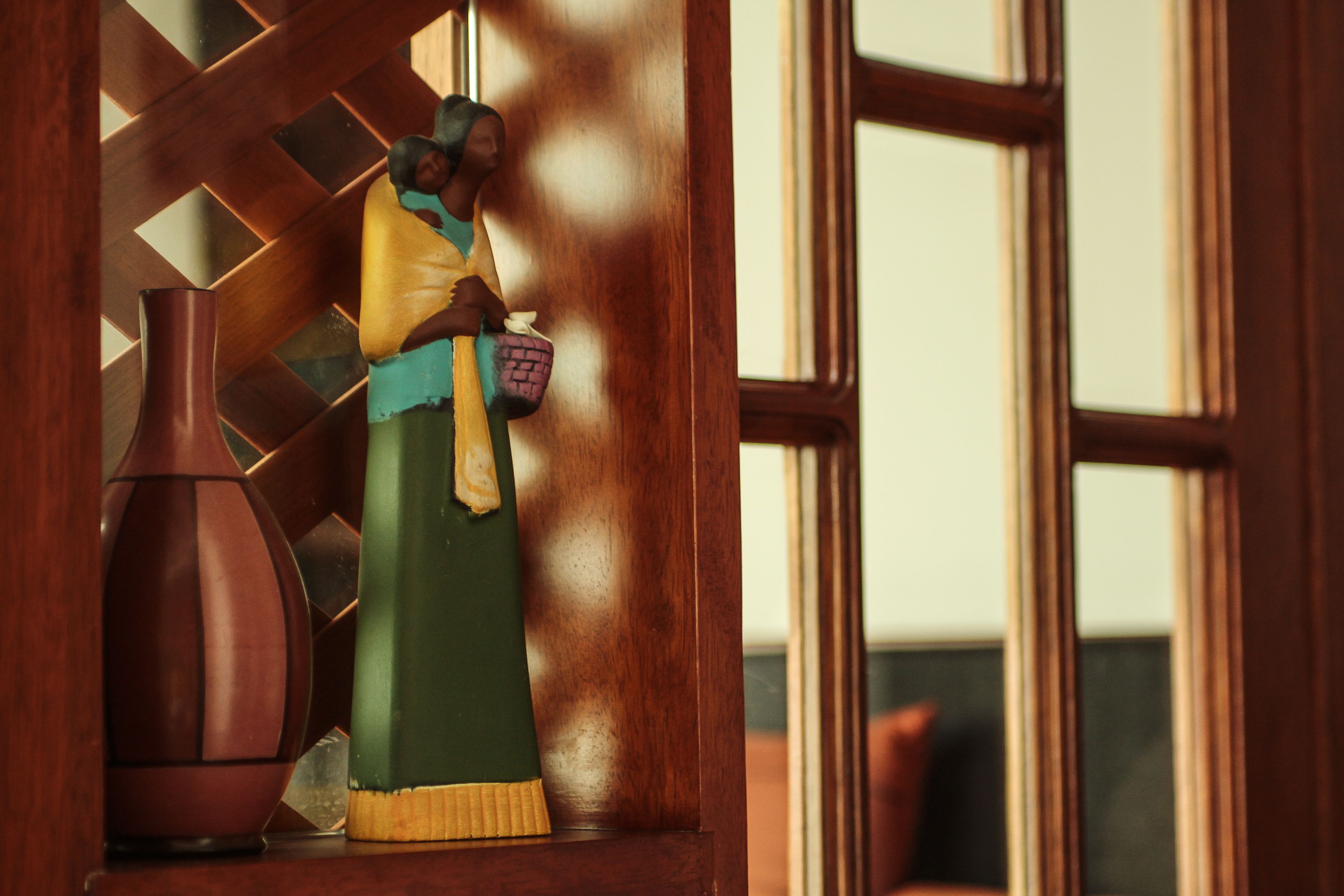 Uma figurina de pessoa vestida com traje típico, um vaso e uma estrutura de madeira com padrão treliçado.