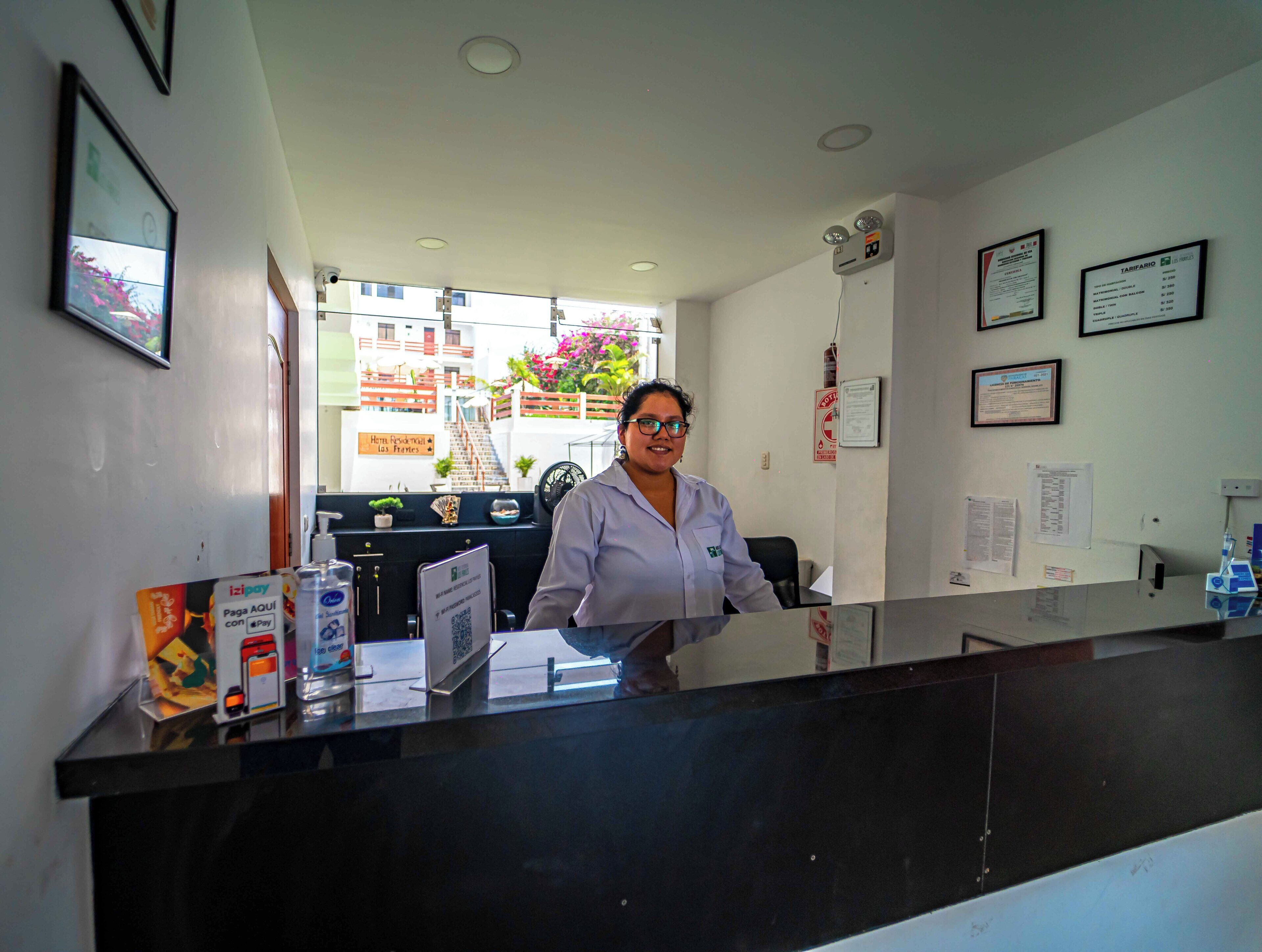 Bancada de recepção com recepcionista, tela digital e diversos cartazes informativos na parede.