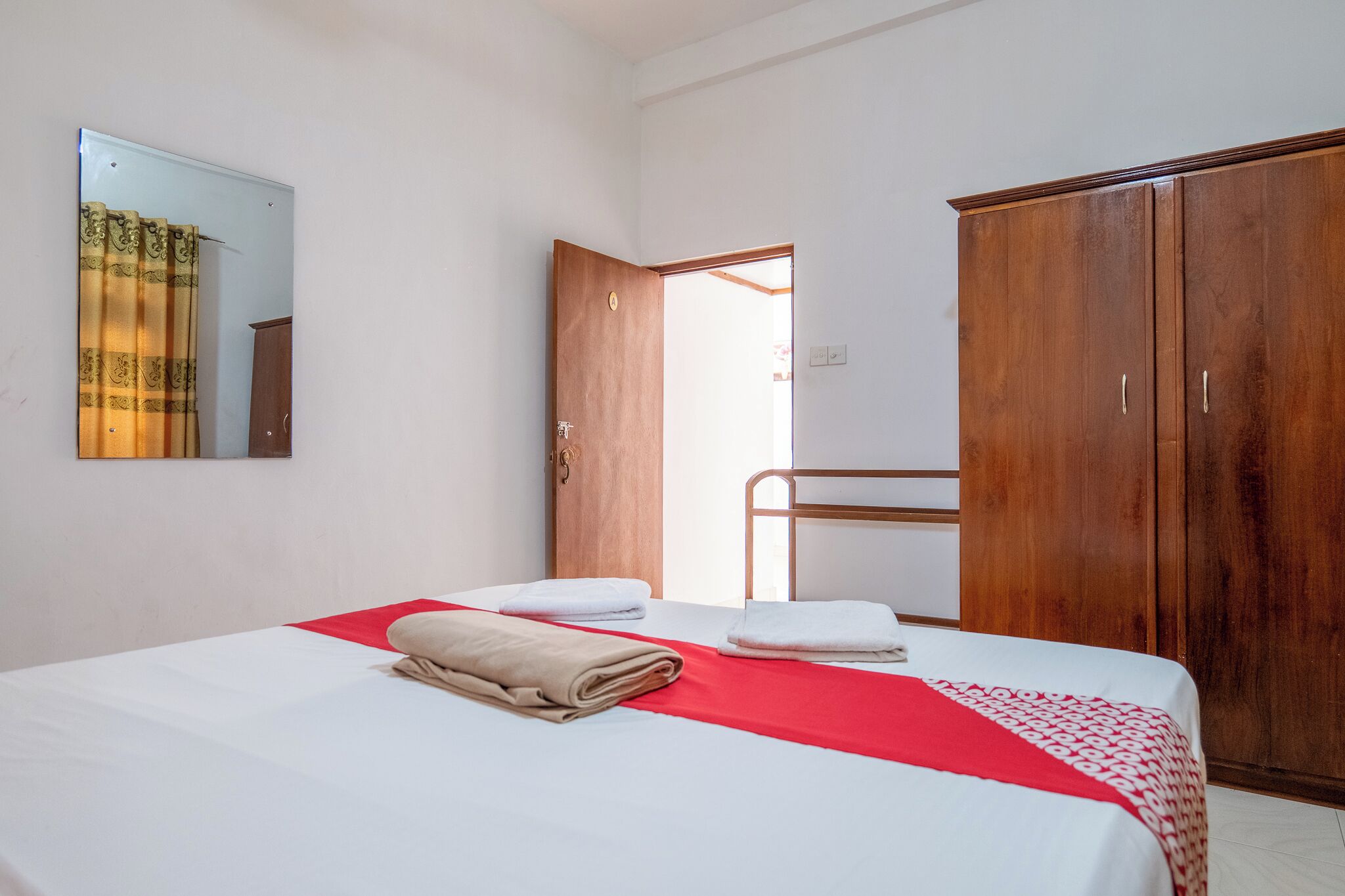 Quarto de hotel com cama, guarda-roupa, espelho e porta que dá para outro aposento.