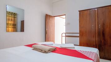 Quarto de hotel com cama, guarda-roupa, espelho e porta que dá para outro aposento.