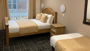 Quarto de hotel com uma cama grande, uma cama menor, mesa de cabeceira, espelho e janela com cortinas.