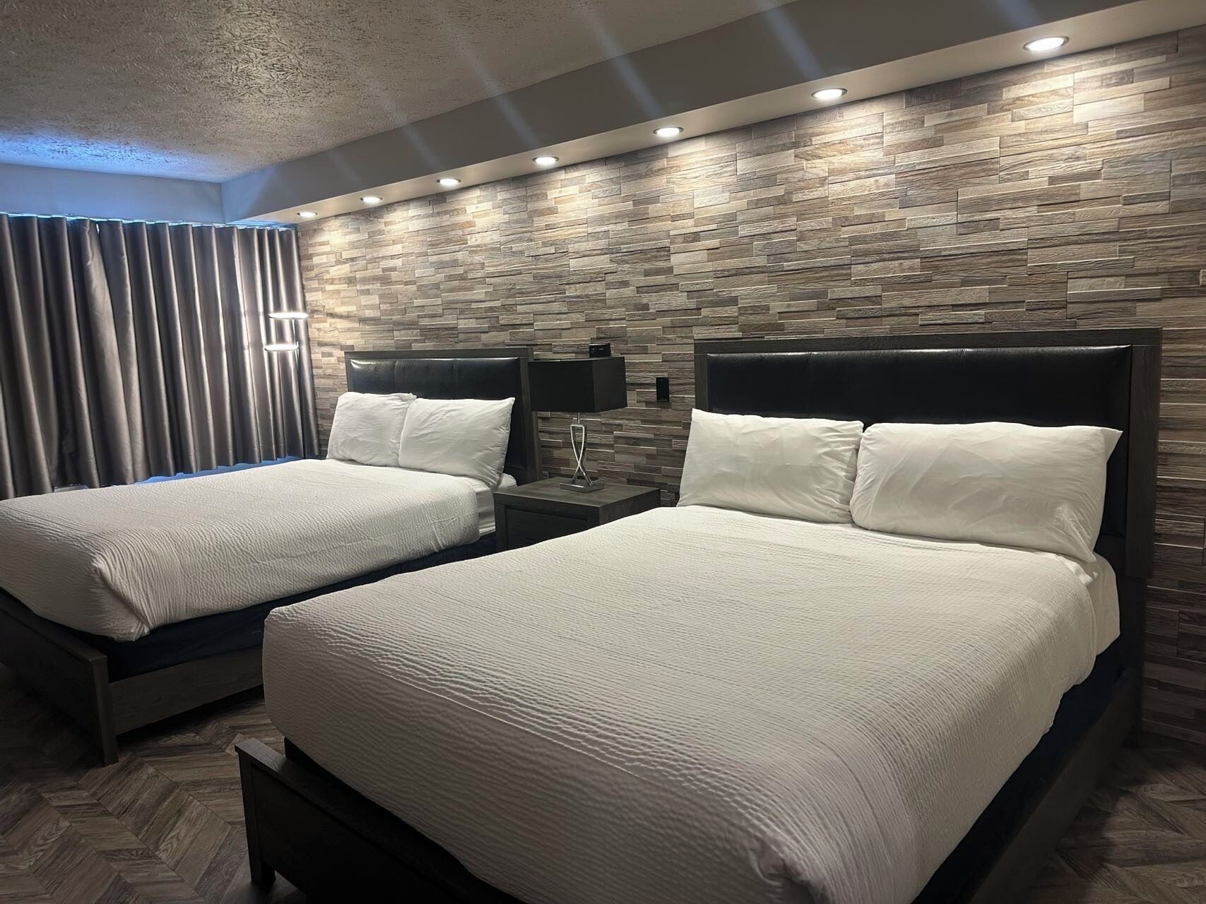 Quarto de hotel com duas camas, design moderno e parede de madeira com padrão losango.