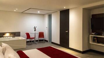Quarto de hotel moderno com cama, escrivaninha, cadeira e mesinha de centro com um vaso.