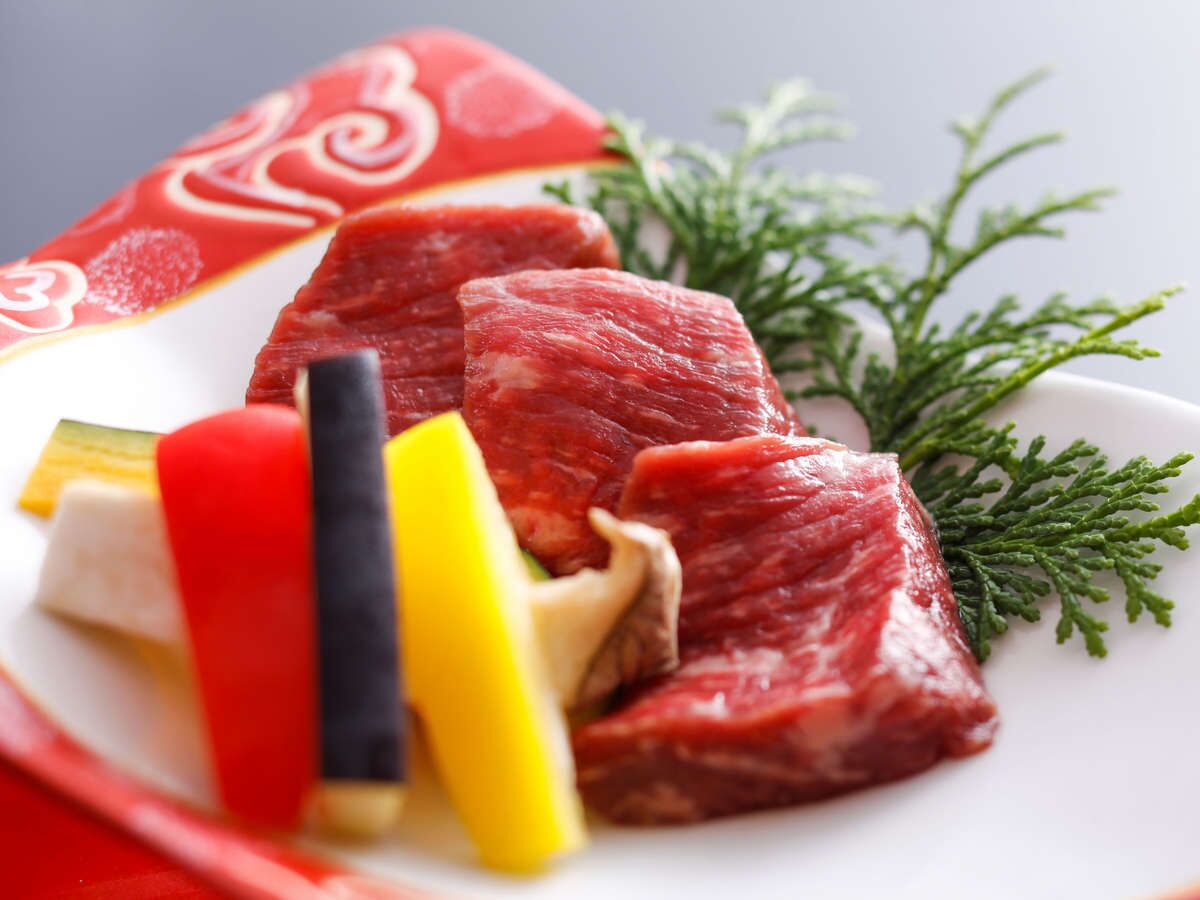 Um prato com carne crua, vegetais e um ramo de folhagem.