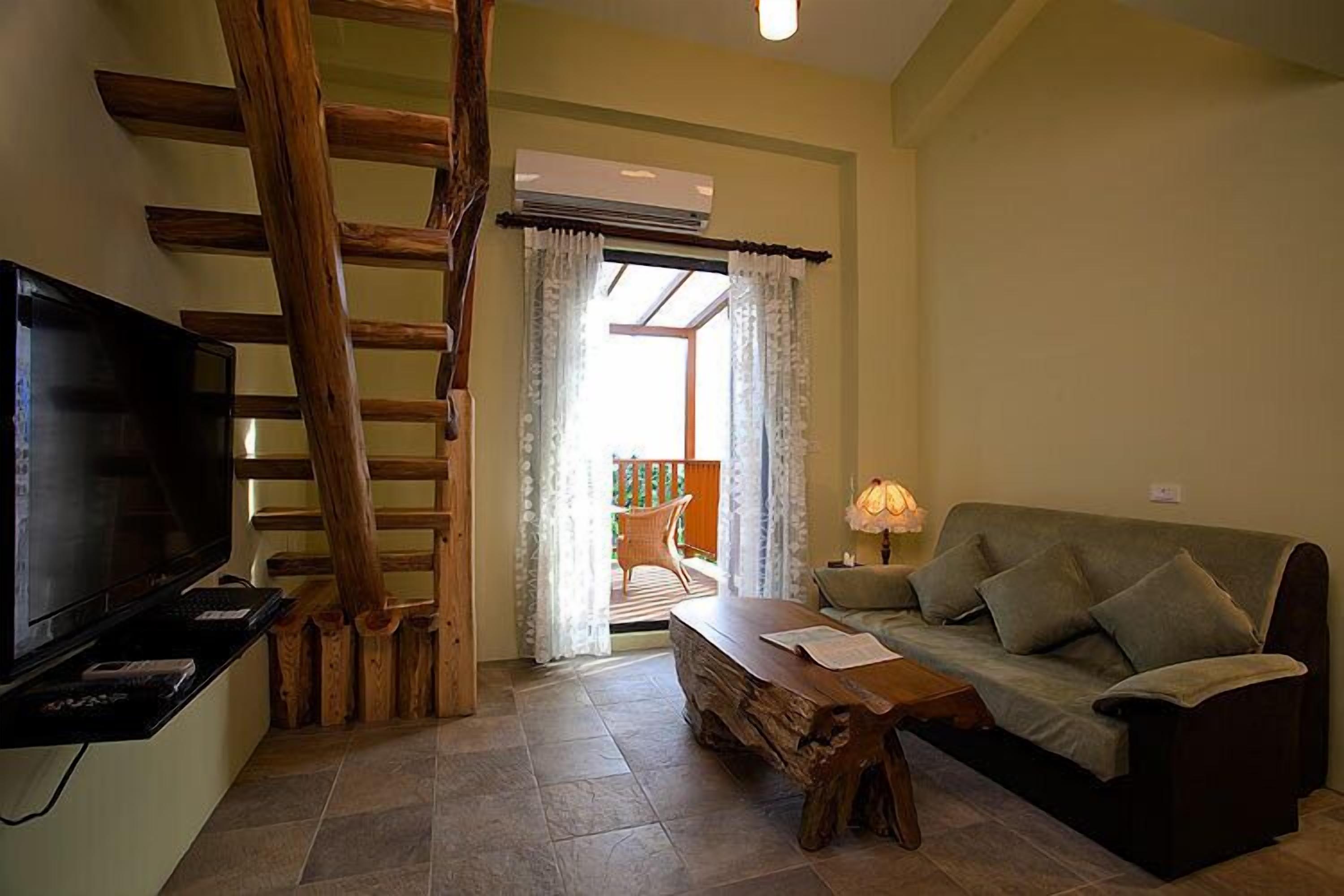 Uma sala de estar com escada de madeira, televisão, sofá, mesa de centro de madeira e aparelho de ar condicionado.