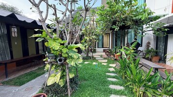 Um pátio com um banco de madeira, plantas em vasos e uma pequena área ajardinada com pedras no chão.