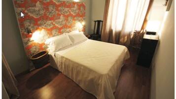 Uma cama bem arrumada com edredom branco e almofadas, cabeceira de madeira com padrão floral e mesa de cabeceira com abajur.