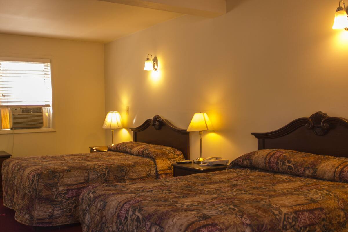 Quarto de hotel com duas camas, cada uma com colcha estampada, duas luminárias de cabeceira, mesas de cabeceira e uma janela com persianas.