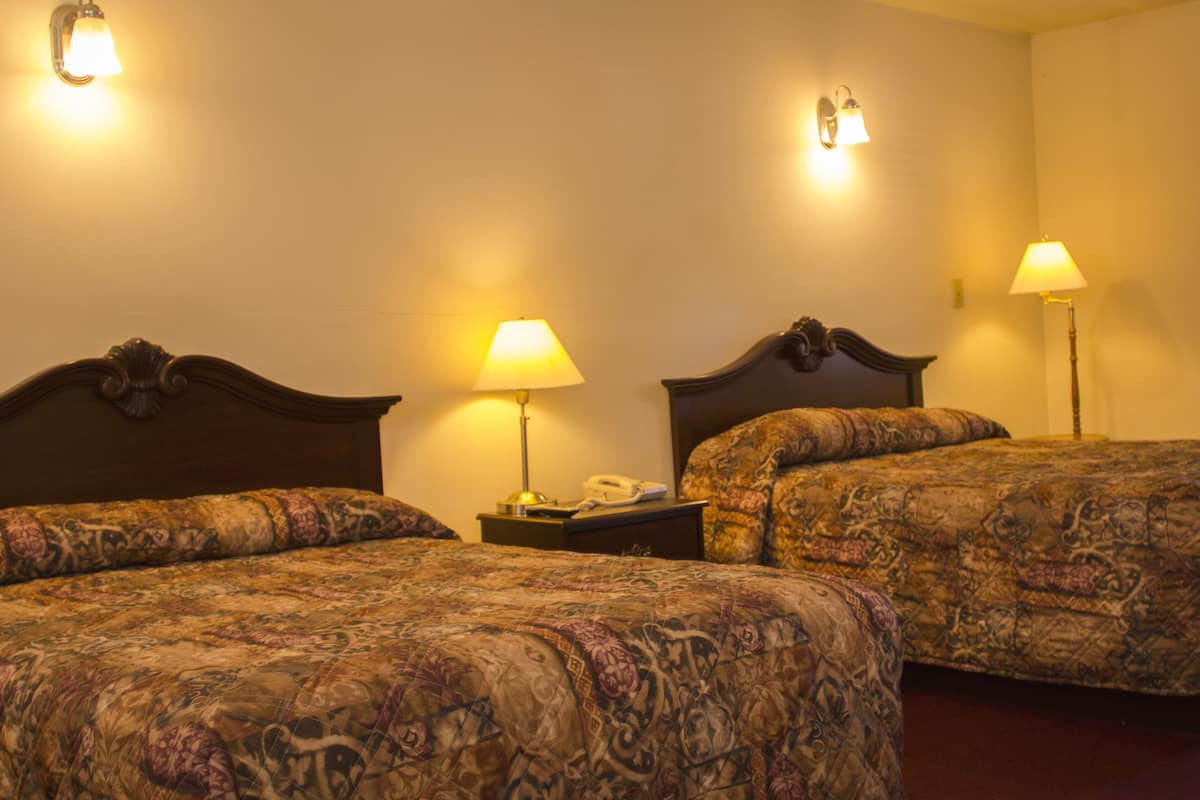 Quarto de hotel com duas camas, cada uma com colcha estampada, luminárias laterais e mesa de cabeceira com telefone.