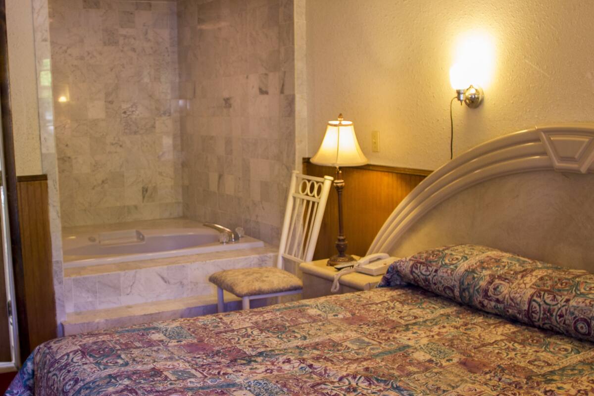 Quarto de hotel com uma cama grande, banheiro com banheira e chuveiro.