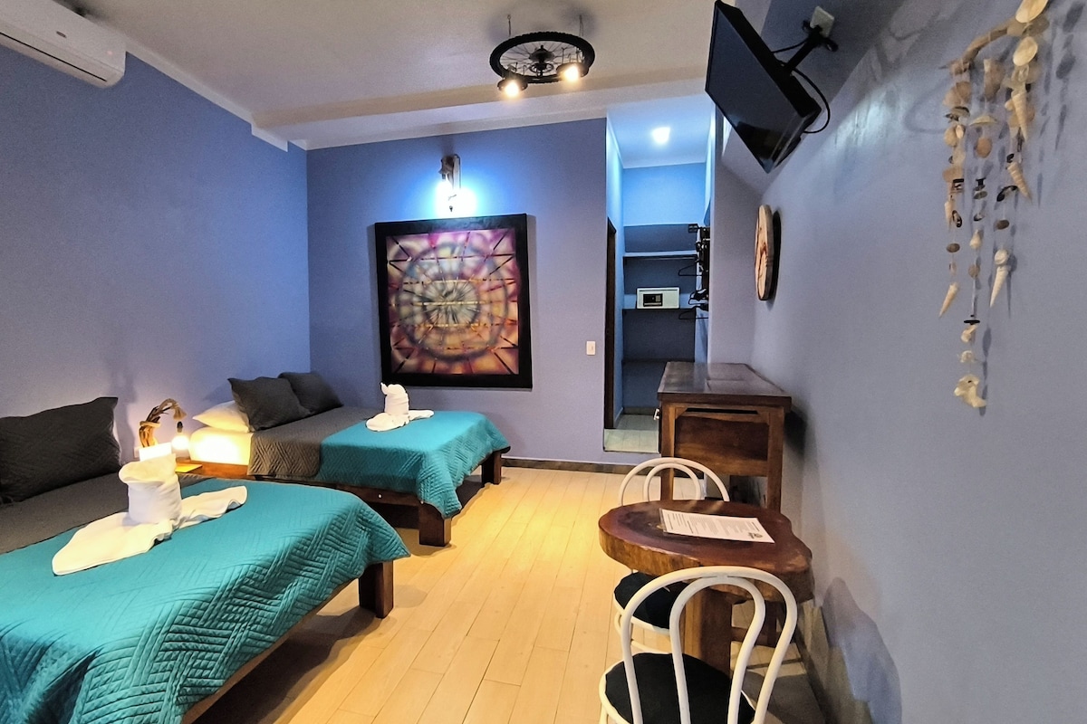 Quarto com duas camas, uma mesinha, uma cadeira, televisão e um painel decorado com relógio e objetos decorativos.