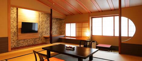 Um quarto japonês tradicional com tatames, uma mesa baixa e uma televisão fixada na parede.