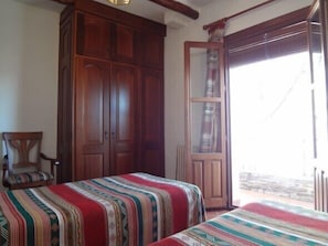 Quarto com duas camas, guarda-roupa de madeira e uma janela grande.