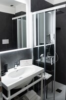 Uma casa de banho moderna com chuveiro em cabine de vidro, uma pia branca e um lavatório.