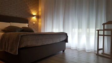 Quarto moderno com parede de tijolos, cama com cabeceira escura e cortinas leves.