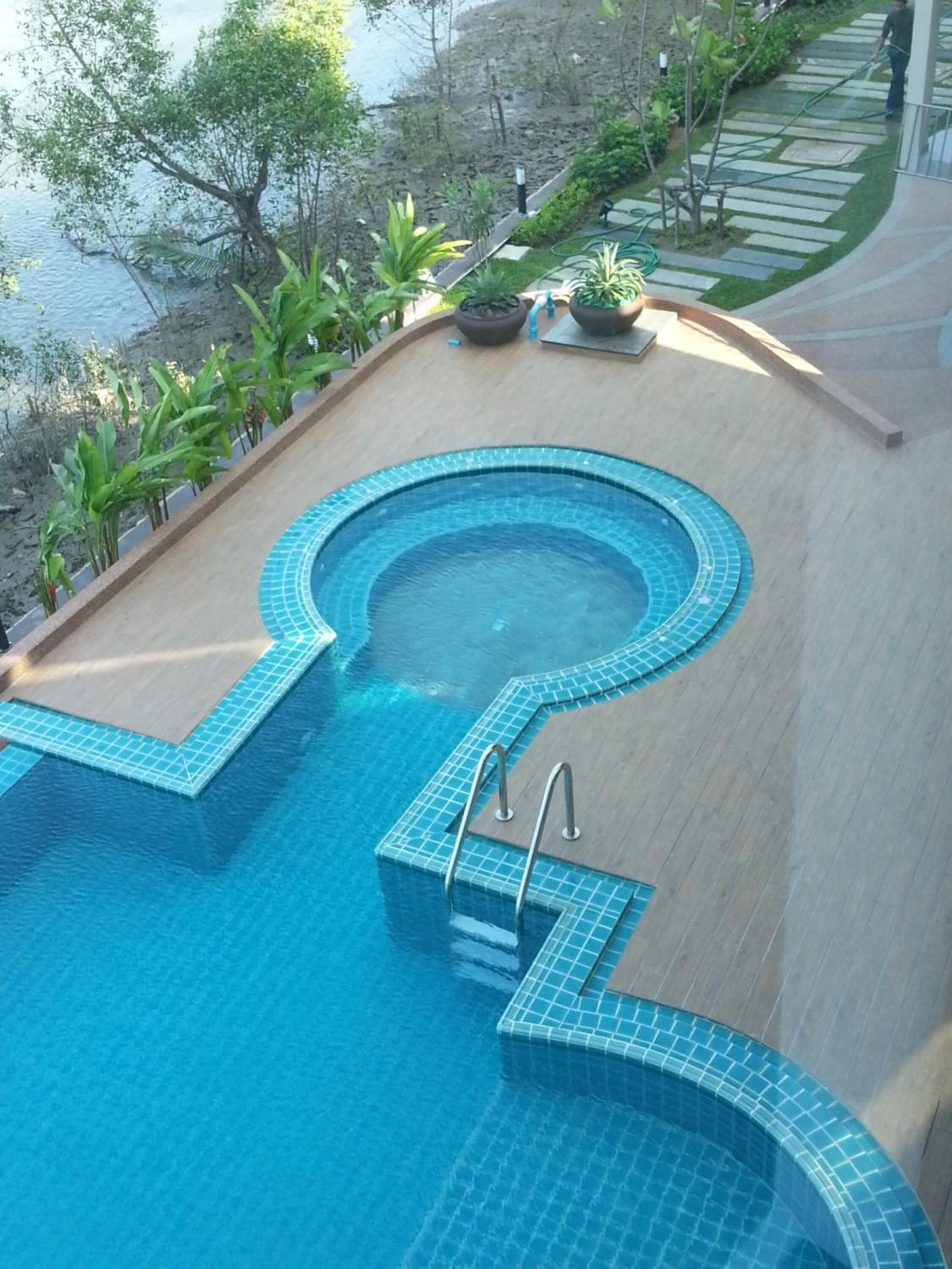 Uma piscina com design circular, cercada por um deck de madeira e vegetação exuberante.