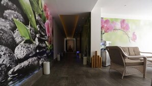 Um corredor com um grande mural floral, uma cadeira de vime e uma escrivaninha com um computador.
