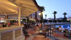 Uma área de bar ao ar livre, com assentos e piscina ao fundo.