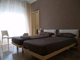 Quarto de hotel com duas camas, uma cadeira e banheiro visível por uma porta aberta.