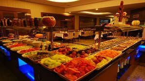 Buffet com diversos alimentos e área de refeições com mesas e cadeiras.
