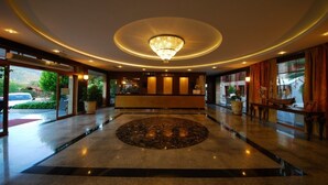 Uma área de recepção de hotel com um candelabro, balcão de recepção e piso de mármore circular.