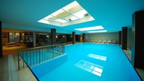Piscina interna com chão azul, guarda-corpo de vidro e luzes no teto.