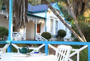 Uma casa branca e azul com varanda, uma mesa com um bule e uma tigela, e uma cadeira.
