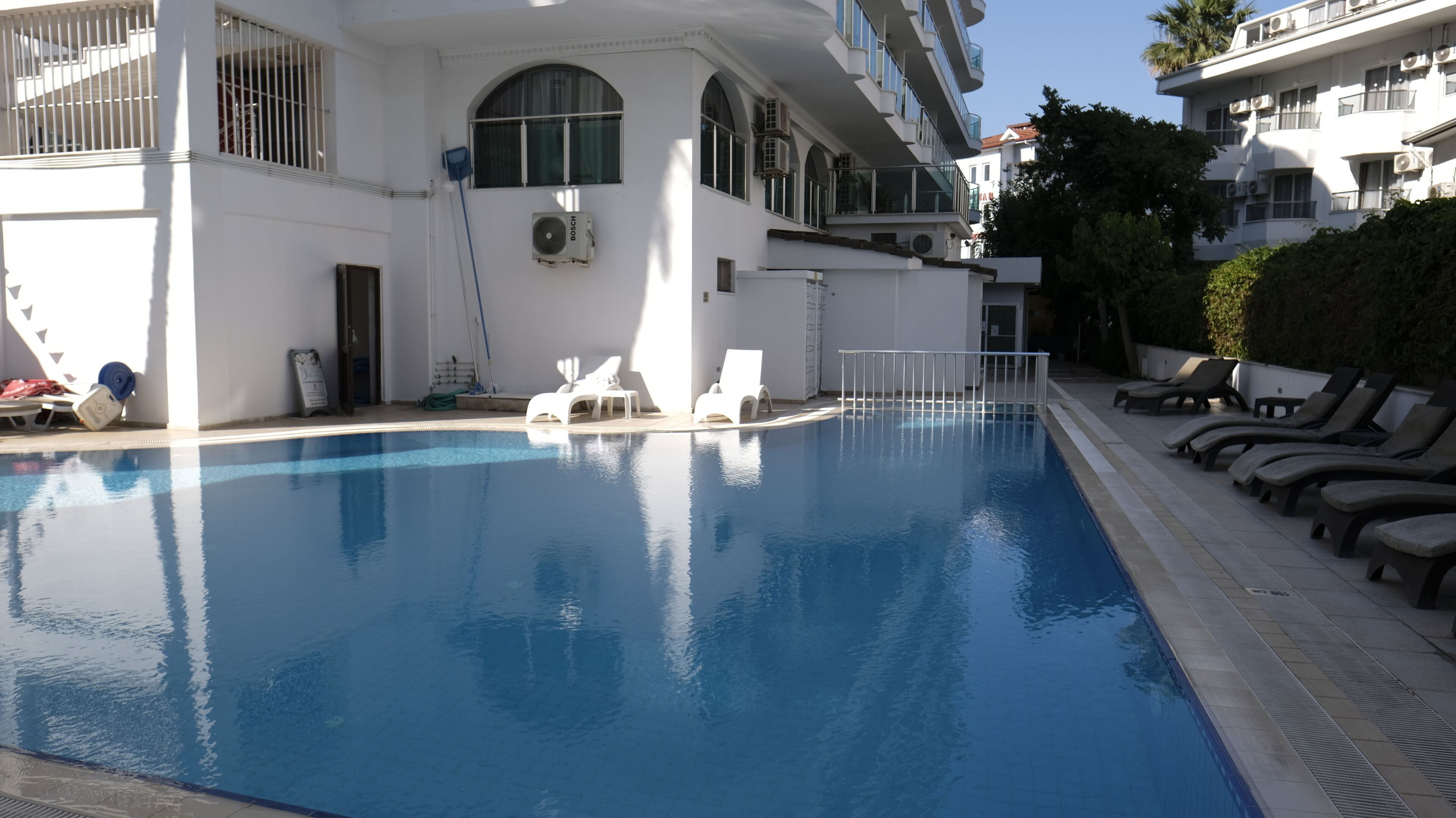 Piscina com espreguiçadeiras e um edifício com várias varandas e janelas.