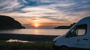 Uma carrinha branca estacionada à beira-mar, com o pôr do sol ao fundo.