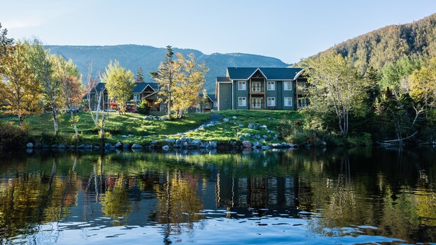 Um imóvel à beira do lago com uma casa grande, um pequeno píer e um reflexo na água.