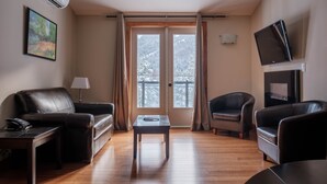 Uma sala de estar com um sofá, cadeiras, uma mesa de centro, uma TV e um quadro na parede.