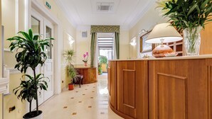 Um saguão de hotel com uma recepção de madeira, plantas em vasos e piso ladrilhado.