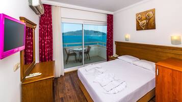 Quarto de hotel com cama, televisão, escrivaninha, telefone e vista para o mar.