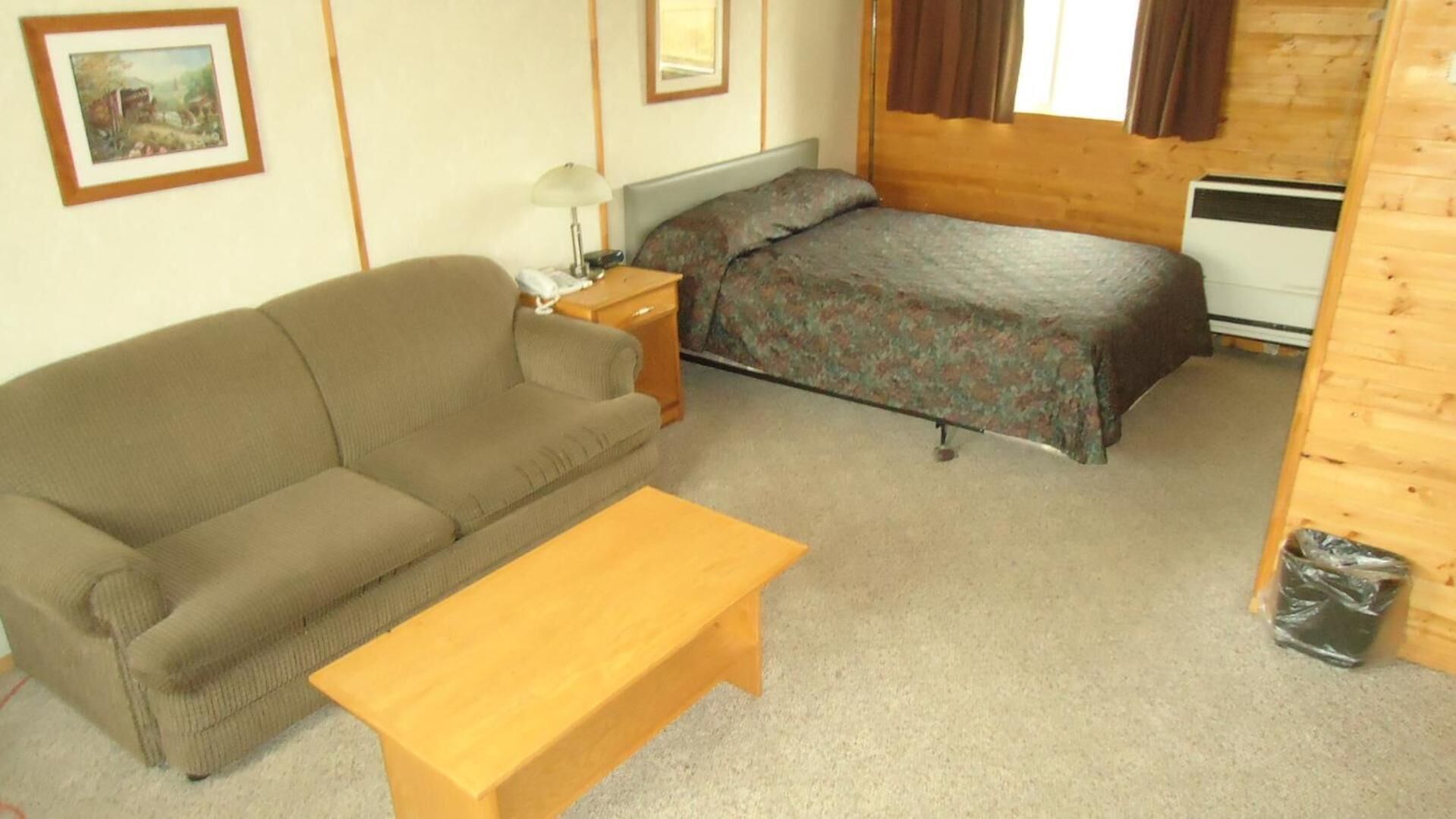 Um quarto pequeno e aconchegante com sofá, uma cama de solteiro, mesa de cabeceira, luminária e mesa de madeira.