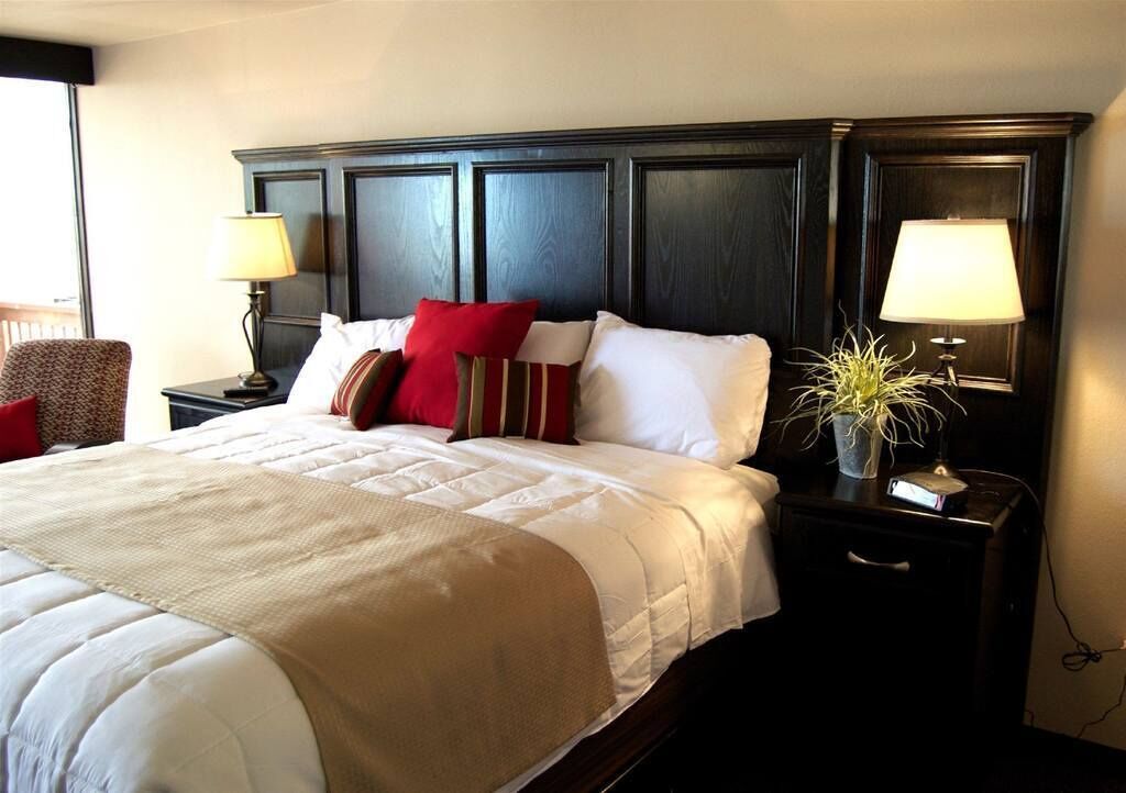 Quarto de hotel com uma cama grande, duas mesas de cabeceira com luminárias, uma cadeira e um vaso de planta.