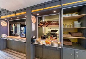 Um balcão de café da manhã com diversos alimentos, utensílios, uma máquina de café e uma seleção de pratos e tigelas.