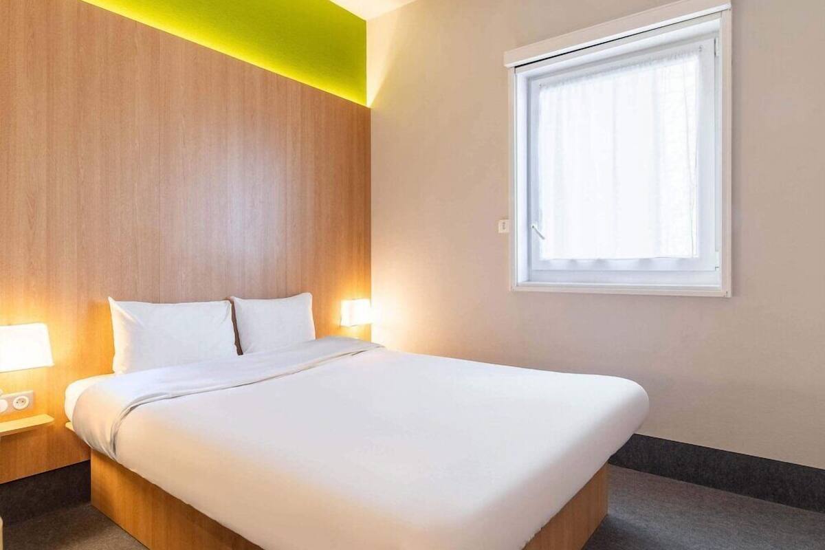 Quarto de hotel com cama, abajures, uma janela e uma parede verde decorativa.