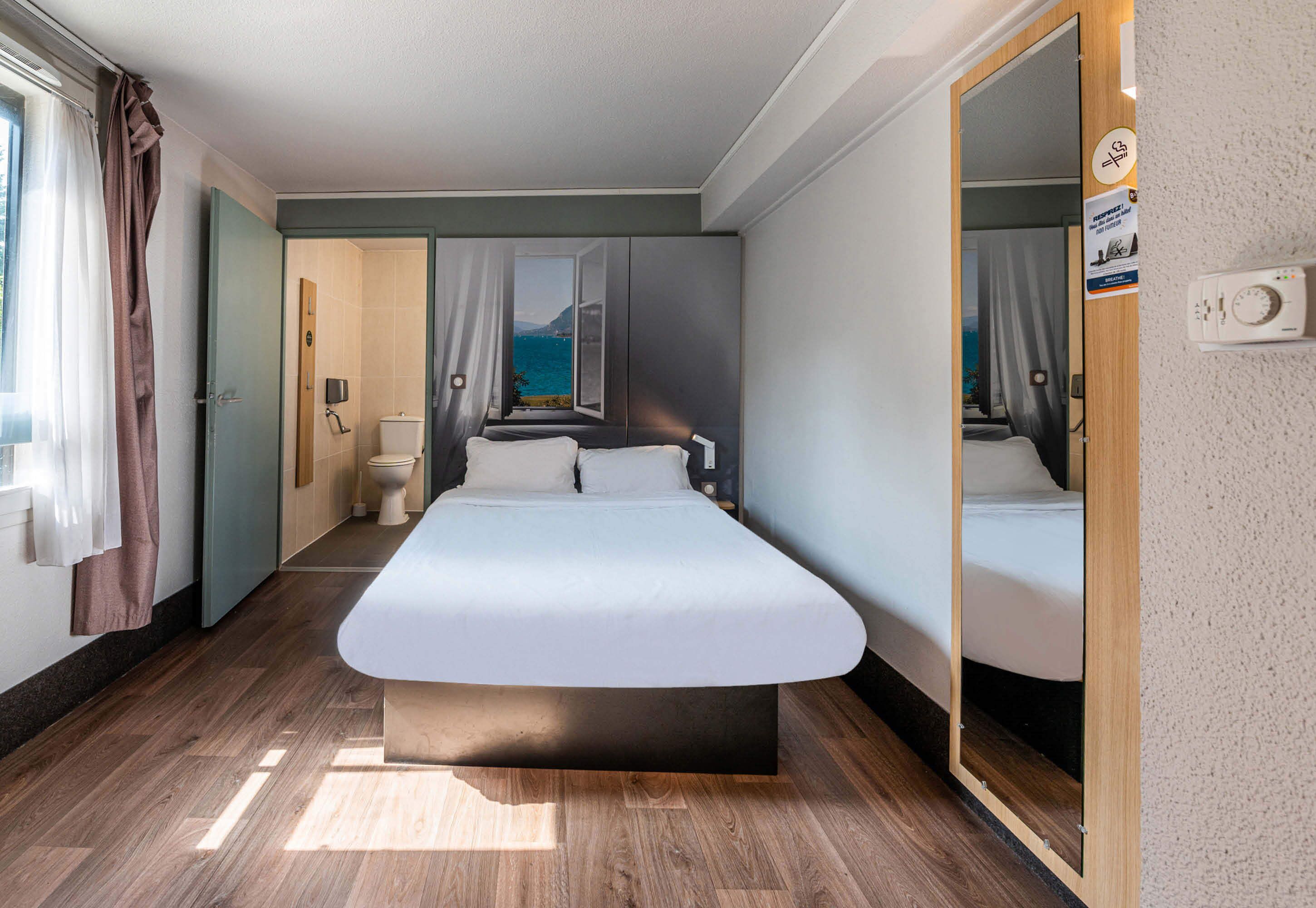 Quarto de hotel moderno com uma cama grande, banheiro com vaso sanitário e chuveiro, e vista para o mar.