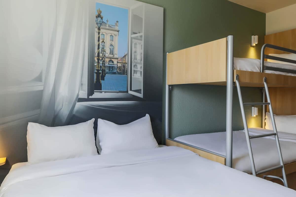 Quarto de hotel com beliche, uma janela grande com vista para um edifício histórico e cortina parcialmente recolhida.