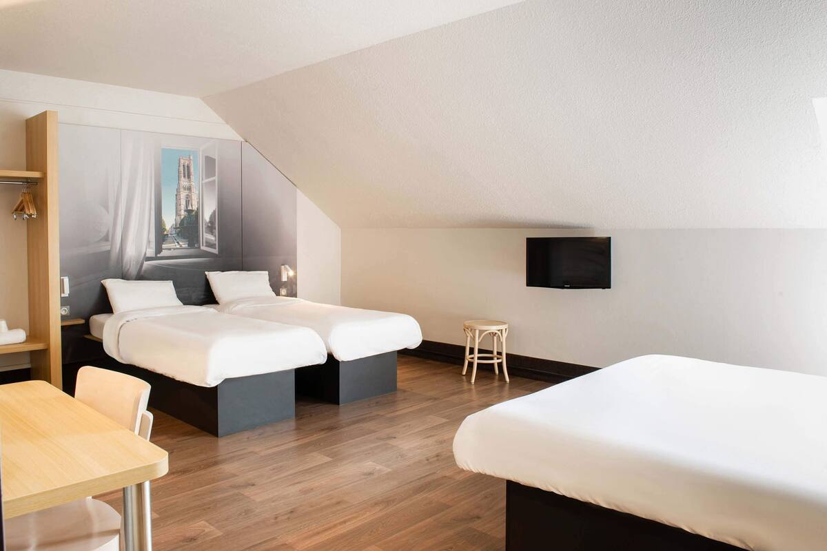 Quarto de hotel moderno com duas camas, uma escrivaninha e um banquinho.