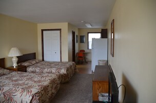 Quarto de hotel com duas camas, uma escrivaninha, uma cadeira, uma televisão e uma porta.