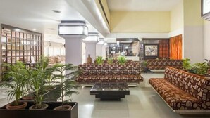 Um hall amplo com sofás estampados, uma mesa de centro e plantas em vasos.