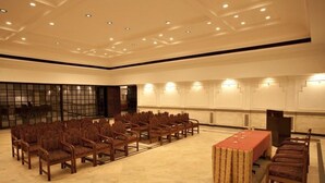 Uma sala de conferências com fileiras de cadeiras de madeira, uma mesa comprida e um pódio.