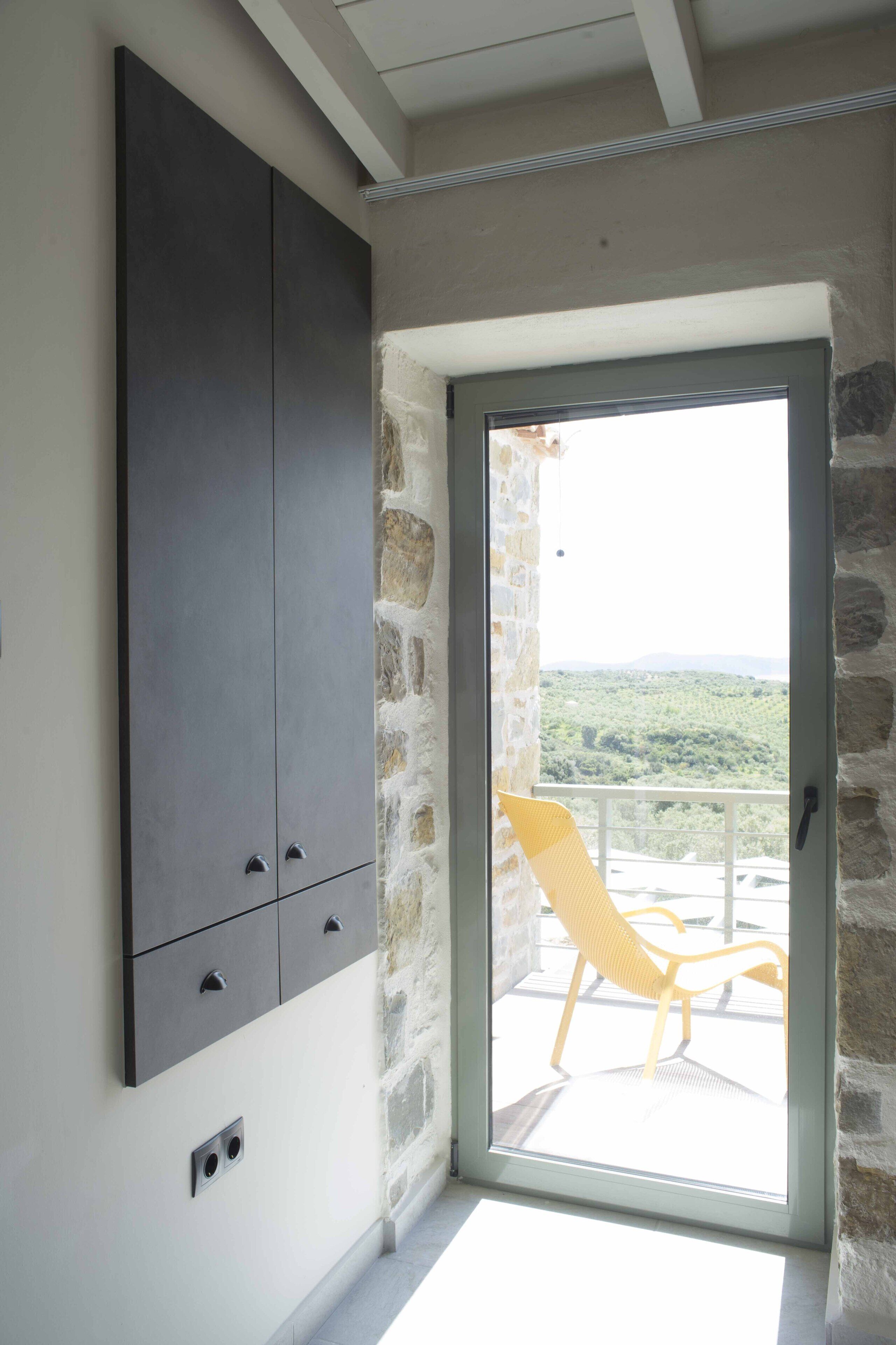 Quarto com guarda-roupa espaçoso, parede de pedra e porta que dá para área externa com uma cadeira.