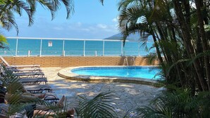 Uma área de piscina com espreguiçadeiras, palmeiras e vista para o mar.