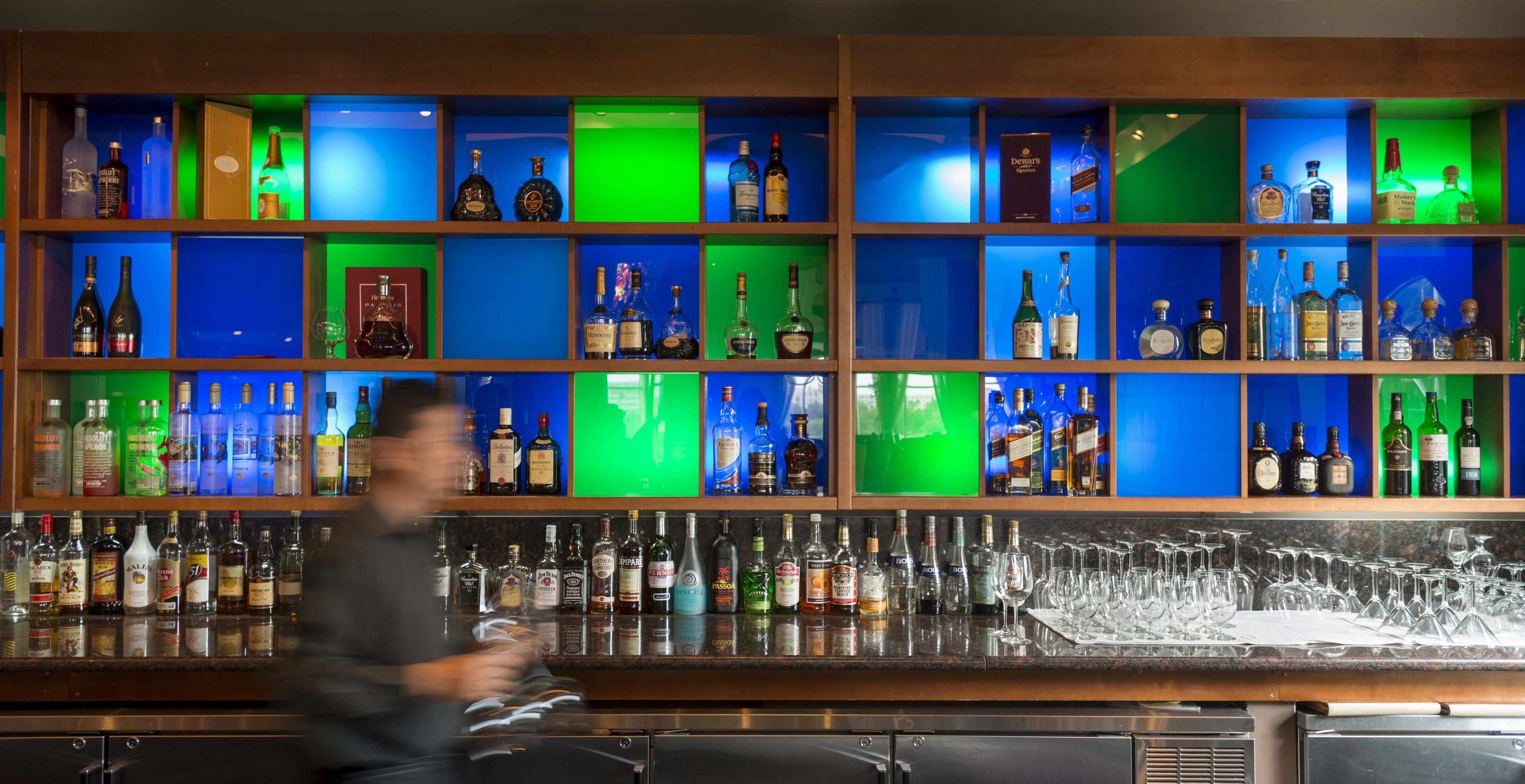 Uma área de bar com prateleiras de garrafas de bebidas e copos.
