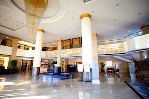 Um hall amplo com pé-direito alto, colunas imponentes e uma fonte central.