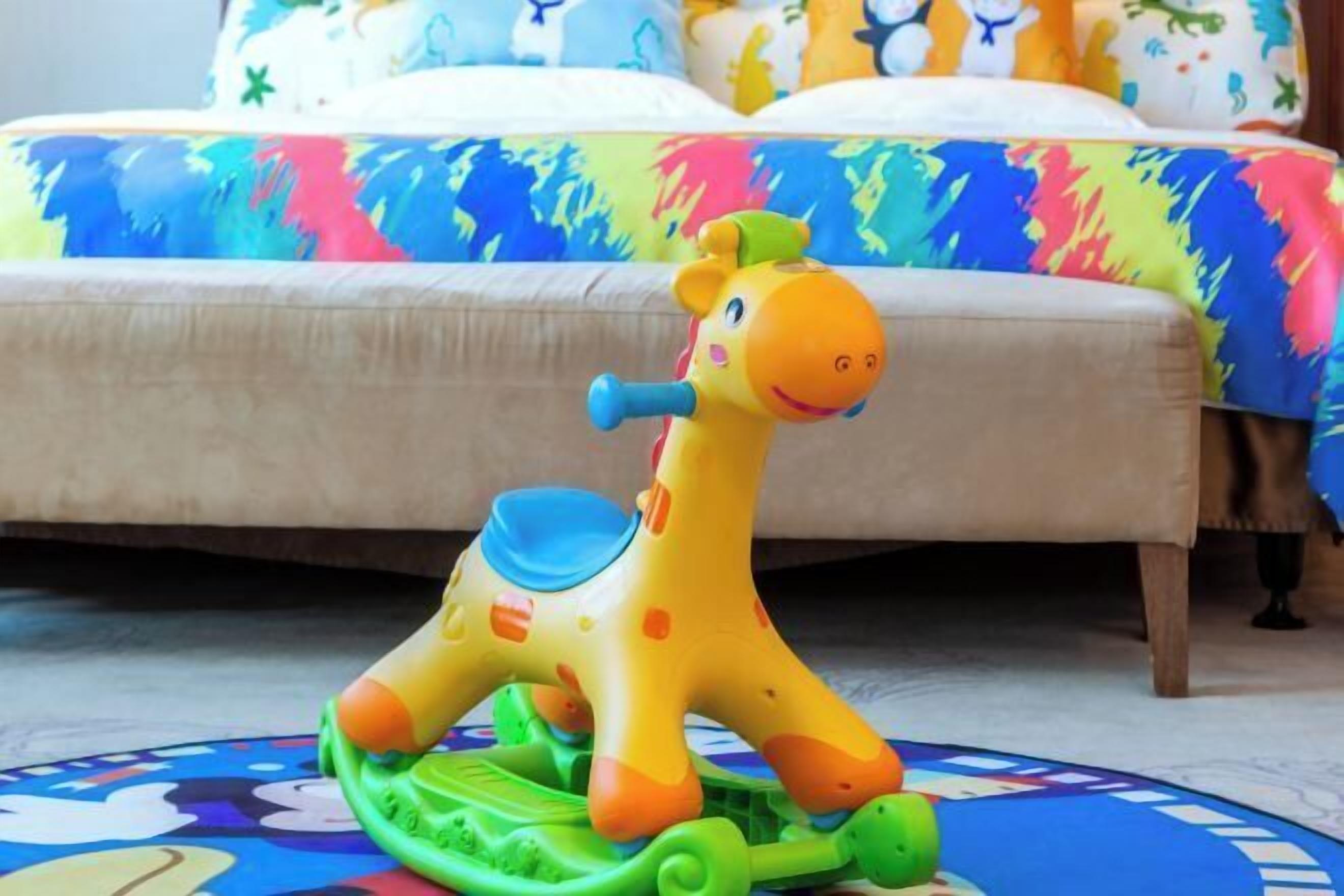 Um brinquedo em formato de girafa sobre um tapete colorido em um quarto com um sofá e almofadas estampadas.